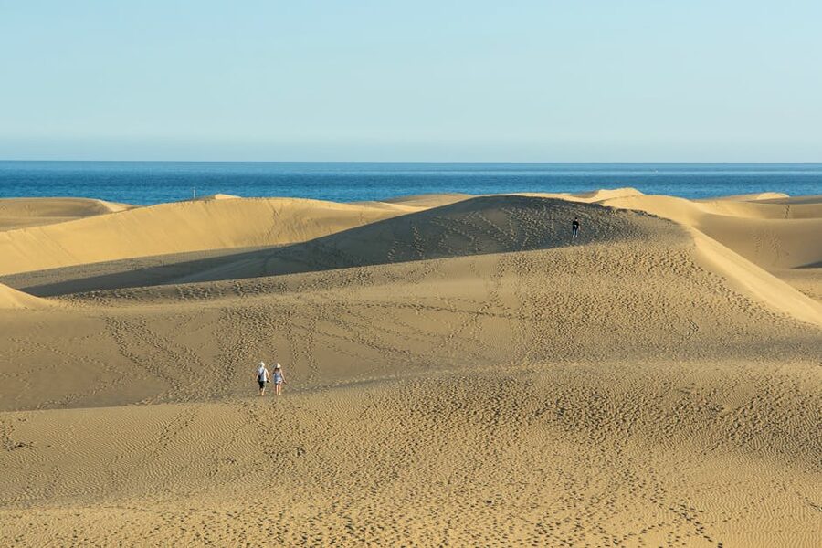 Couple walking across Maspalomas dunes with sea behind them