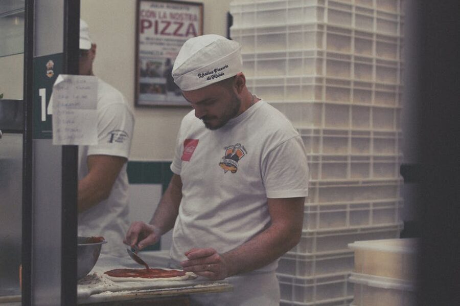 Pizzaiolo spreading sauce on dough in Naples