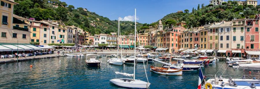 Boats docked at Portofino harbor on a sunny day with pastel buildings behind