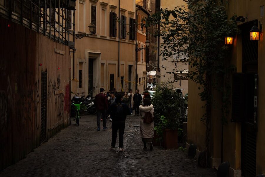 People walking down a cobblestone alley in Rome at evening