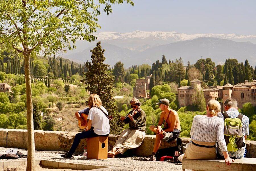 Street musicians performing at a Granada viewpoint with the Alhambra and Sierra Nevada