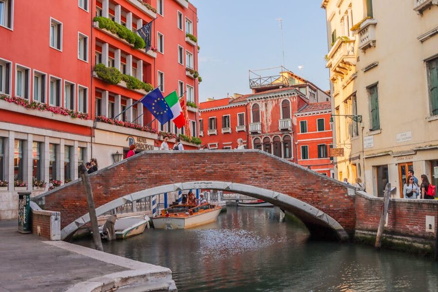 A small Venice bridge with flags and a canal underneath